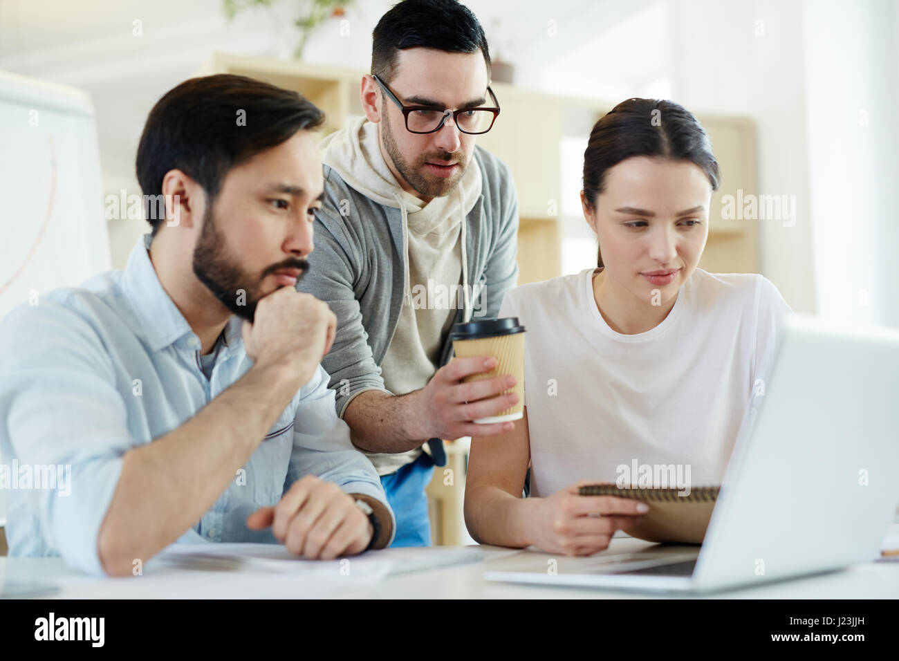 Group of focused business people looking at laptop screen while working ...
