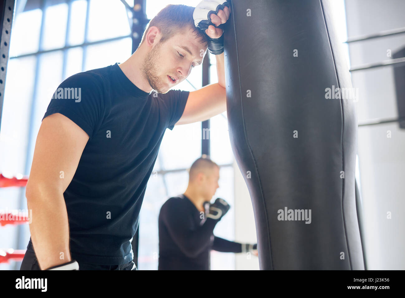 Low angle portrait of young tired sports man leaning on punching bag ...