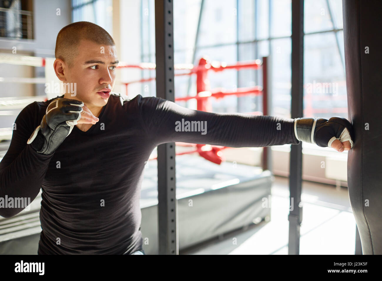 Side view portrait of young muscular sports man hitting punching bag ...