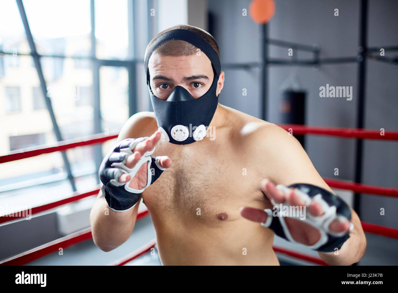 Portrait of shirtless boxer looking at camera while fighting in ring ...