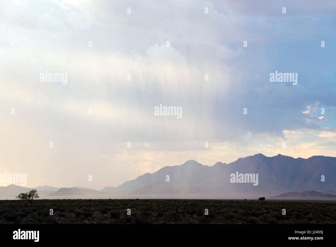 Rain starts to fall from the clouds over the rugged desert landscape ...