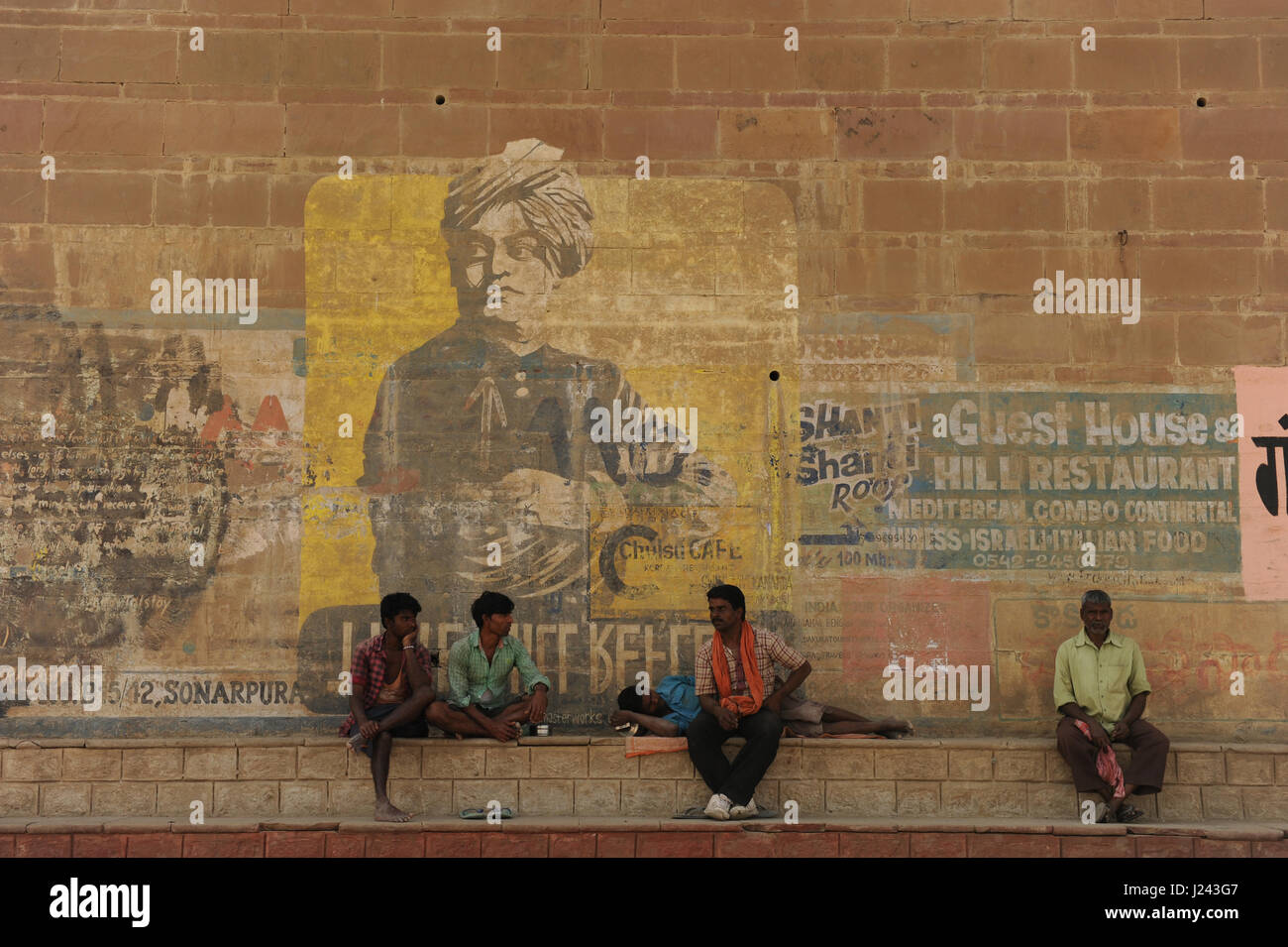 Five men rest by a wall on which shows colourful advertising for hotels ...