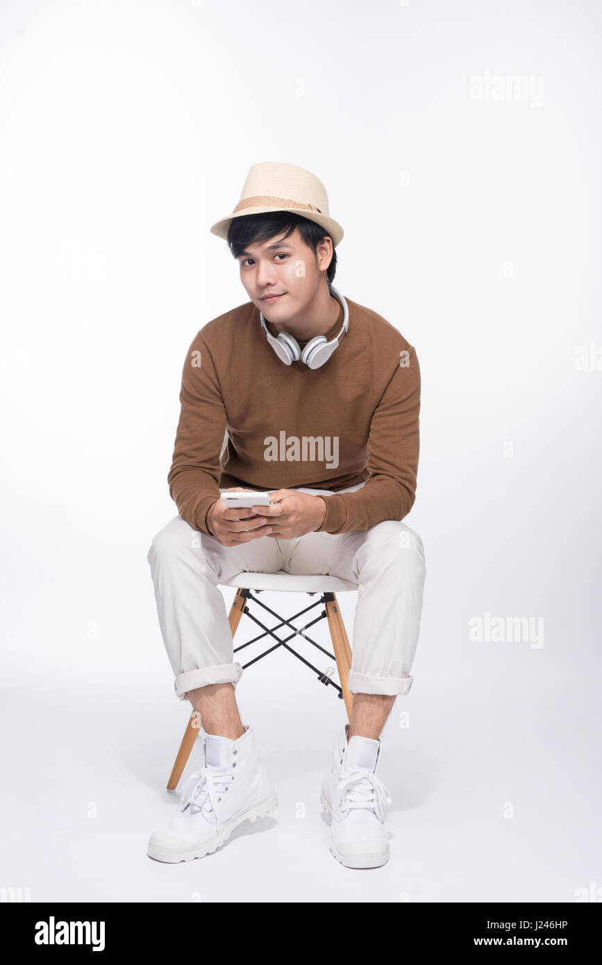 Smart casual asian man seated on chair, holding smartphone in studio ...