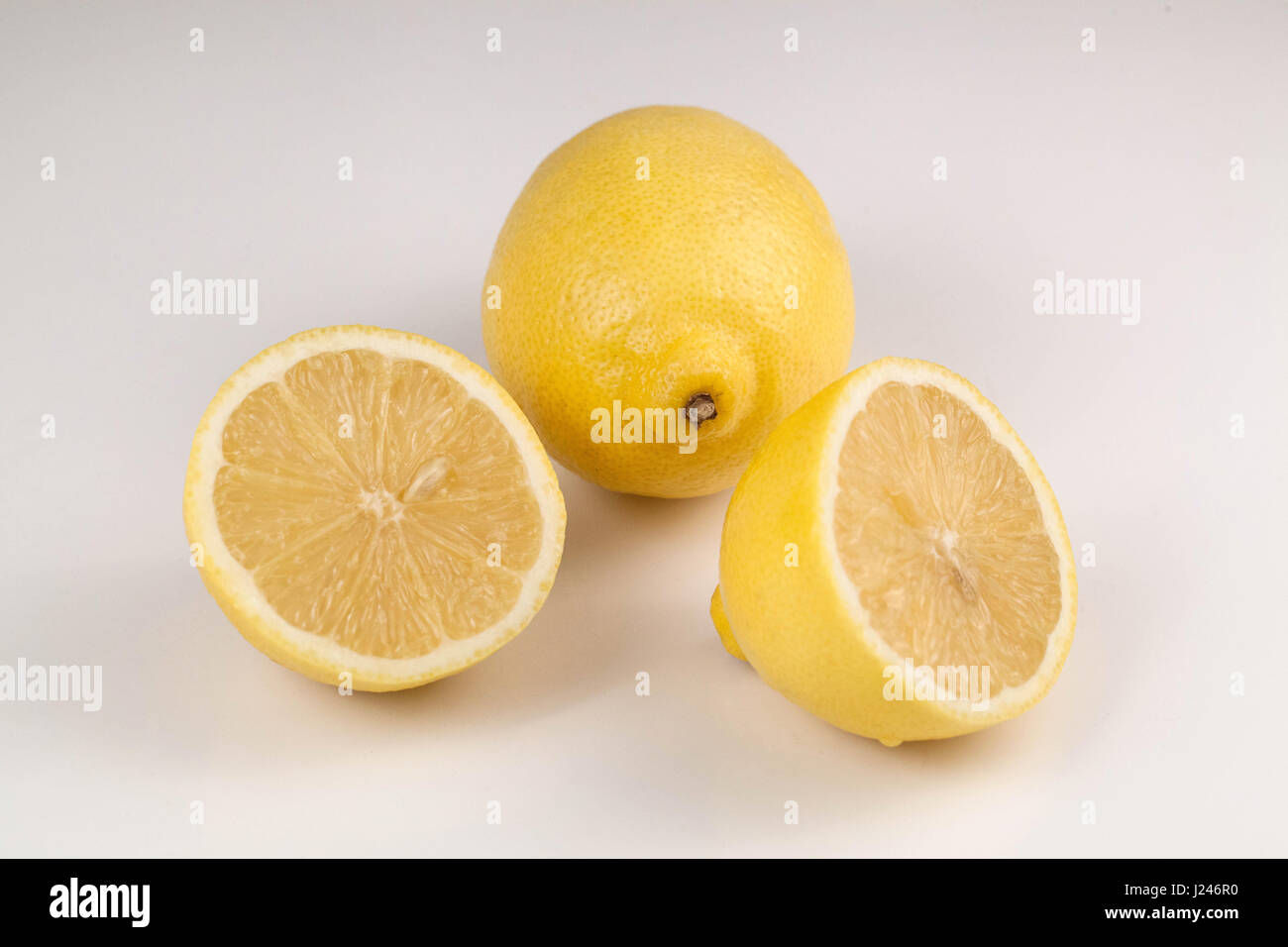 Two ripe lemons on of which is cut into halves placed on a white ...