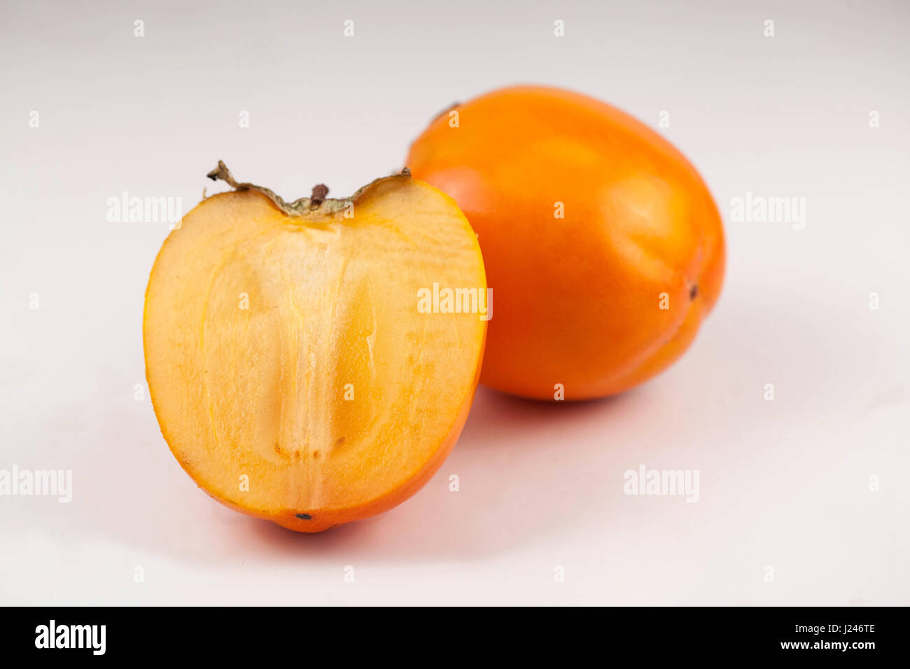 Fresh persimmons one of which cut into half placed on a white surface ...