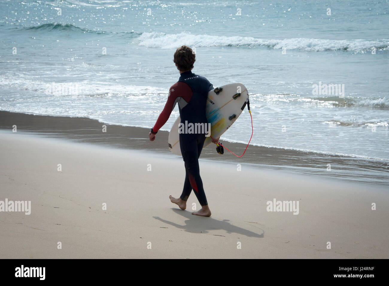 Surfer walking along the beach carrying a surfboard Stock Photo - Alamy