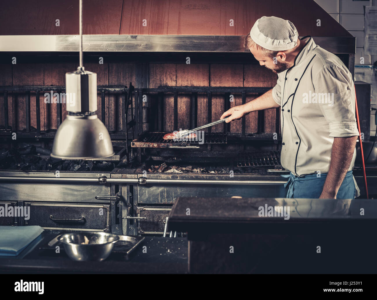 Food concept. Young chef in white uniform monitors the degree of ...