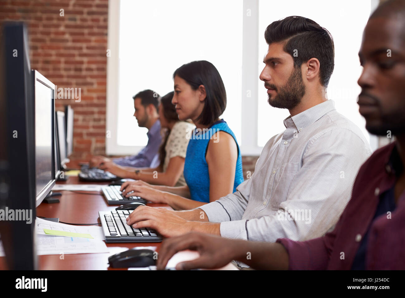 Staff Sitting At Desks Using Computers In Busy Office Stock Photo - Alamy