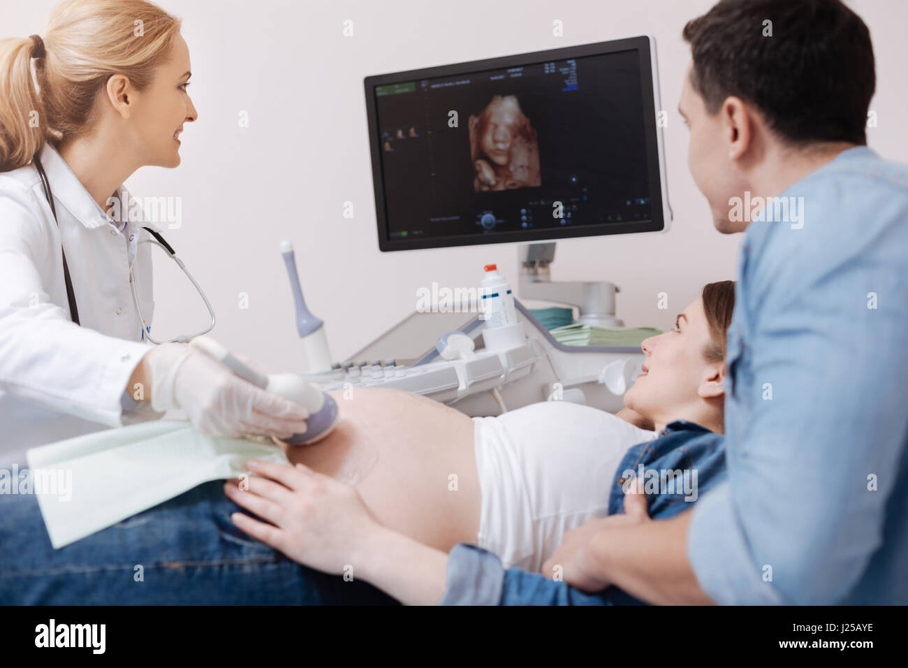 Cheerful medic providing ultrasound scanning of pregnant belly at work ...