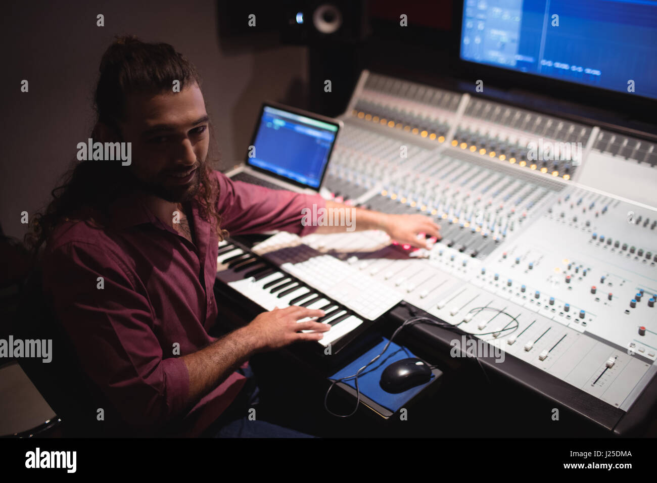 Male audio engineer playing electric keyboard while using sound mixer ...