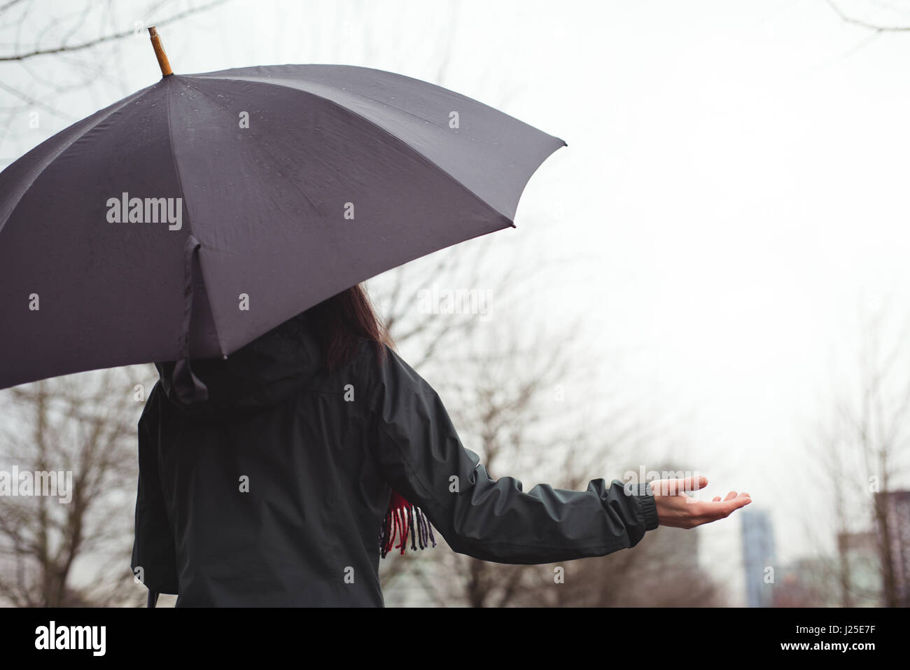 Rear view of woman enjoying rain while holding umbrella during rainy ...