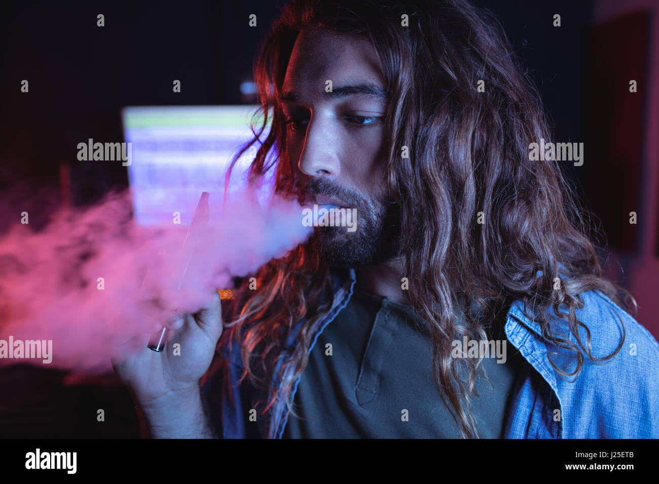 Male audio engineer smoking electronic cigarette in recording studio ...