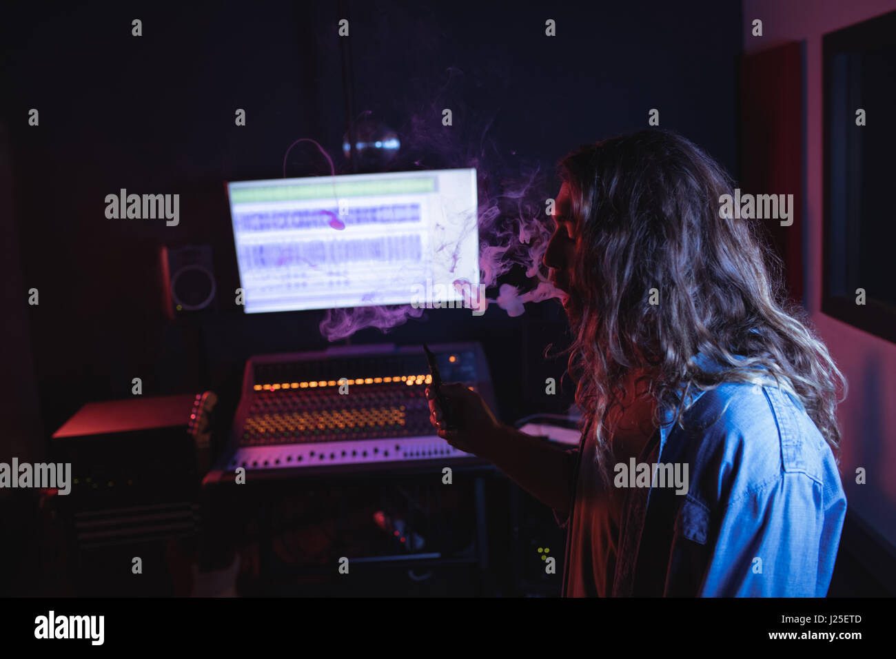 Male audio engineer smoking electronic cigarette in recording studio ...