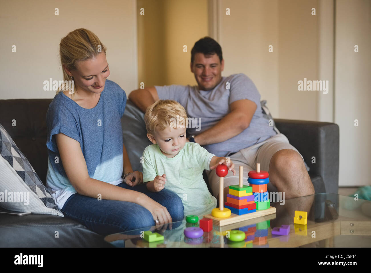 Parents watching boy playing with stacking toy in living room at home ...