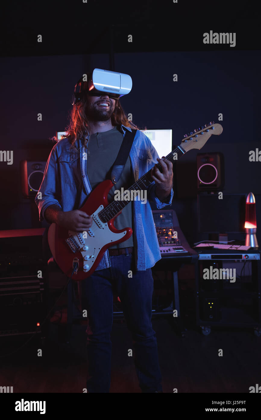 Male audio engineer using virtual reality headset while playing guitar ...