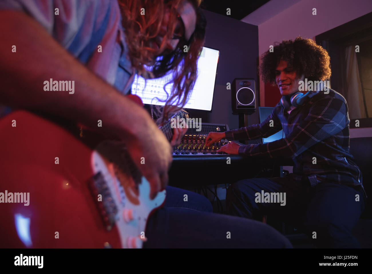 Male audio engineer playing electric guitar with colleague in ...