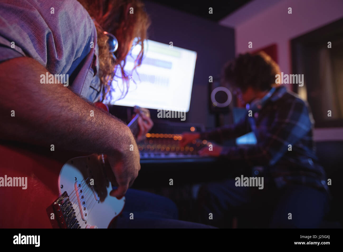 Male audio engineer playing electric guitar with colleague in ...