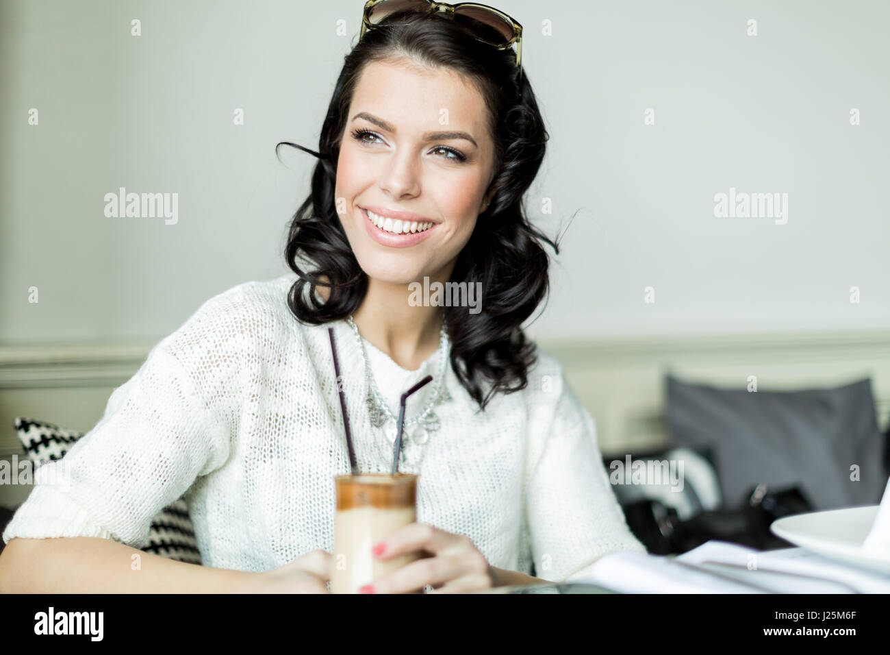 Beautiful young lady smiling in a restaurant while holding her coffee ...