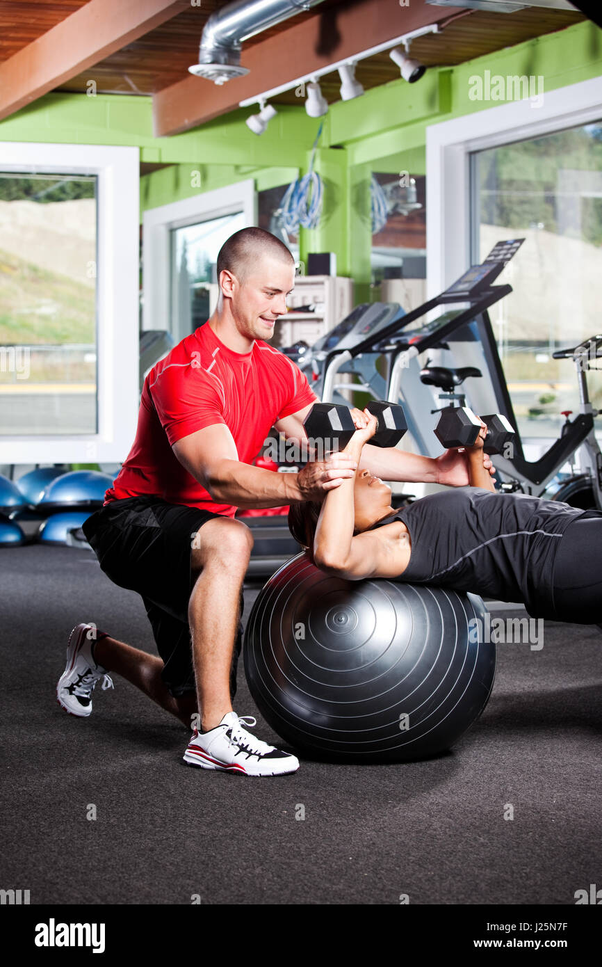 A shot of a male personal trainer assisting a woman lifting weights ...