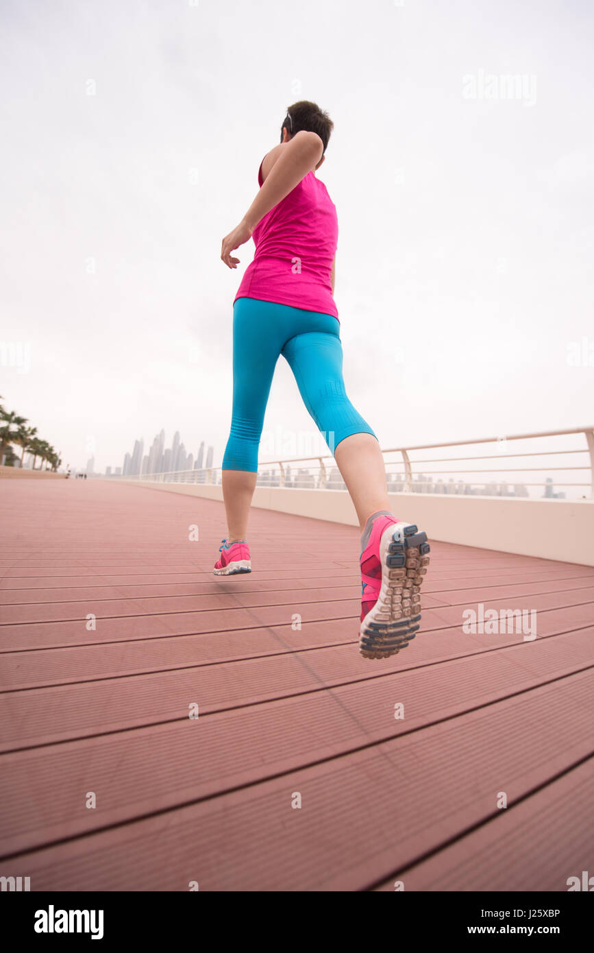 very active young beautiful woman busy running on the promenade along ...