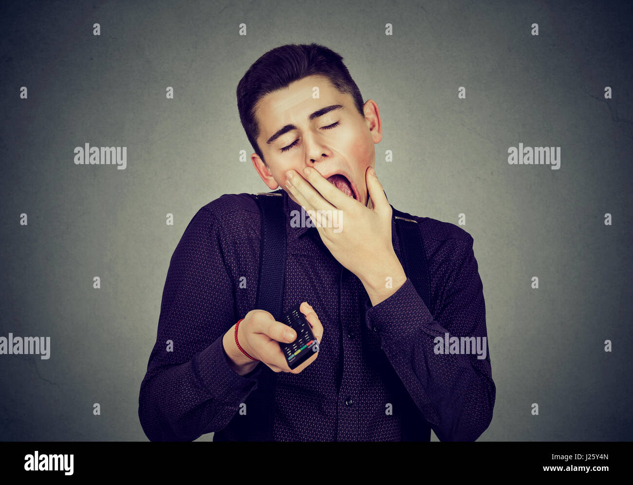 Young bored man yawning changing the channel with the remote control ...