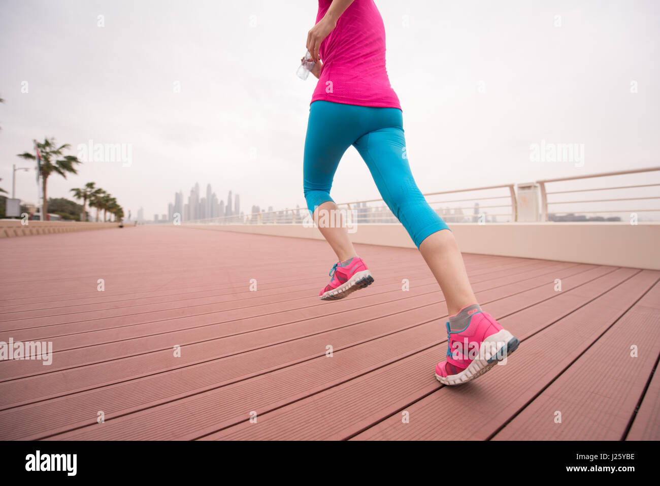 very active young beautiful woman busy running on the promenade along ...