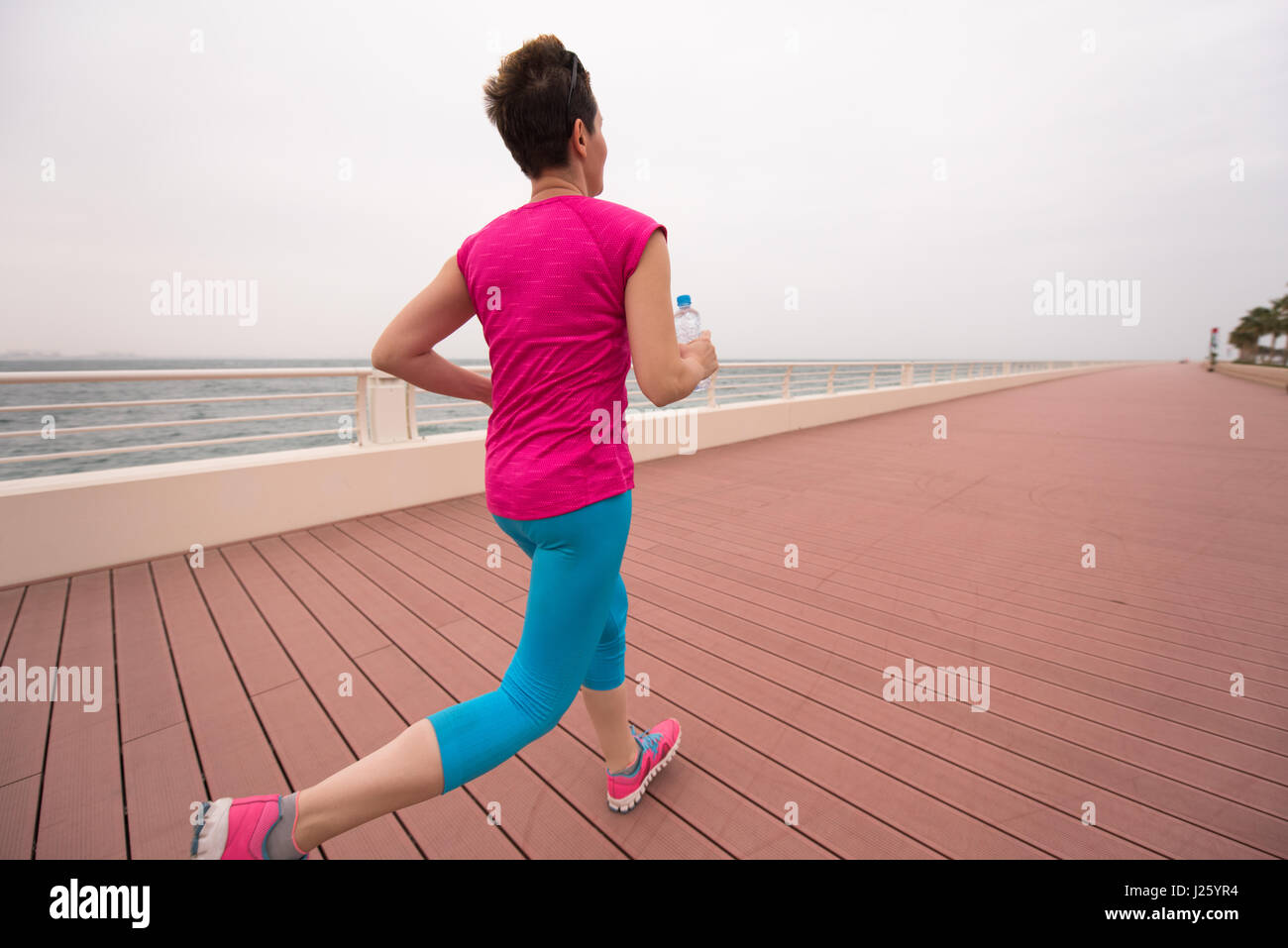 very active young beautiful woman busy running on the promenade along ...