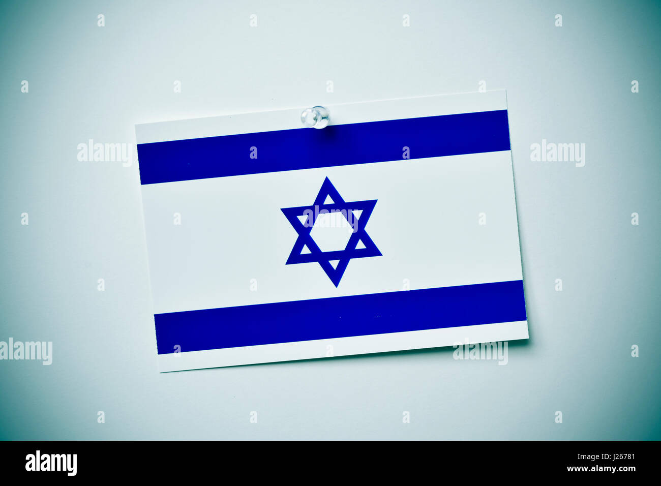 closeup of a flag of israel pinned with a push-pin to an off-white ...