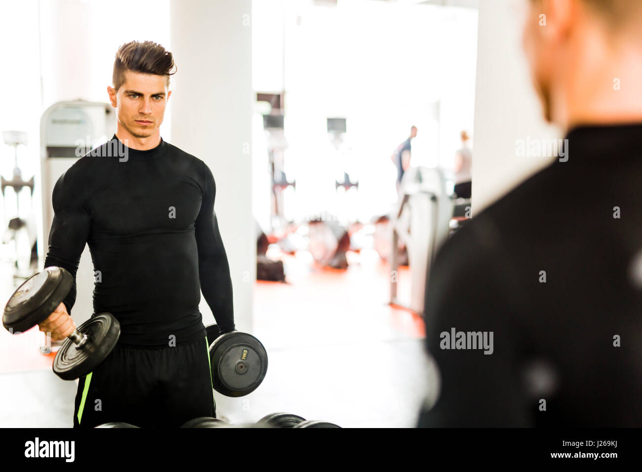 Young muscular man working out in a gym and lifting weights with his ...