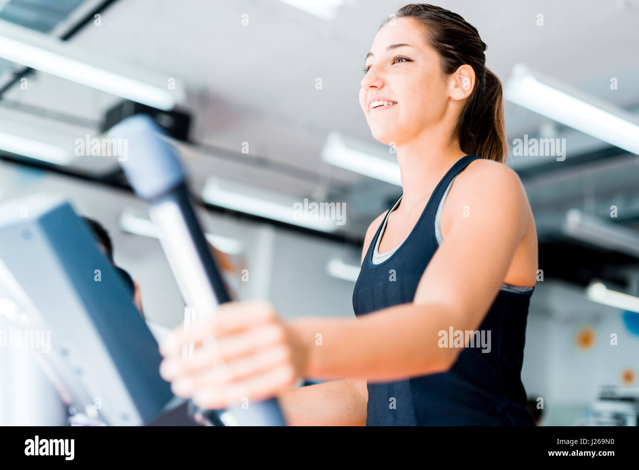 Beautiful young lady using the elliptical trainer in a gym in a ...