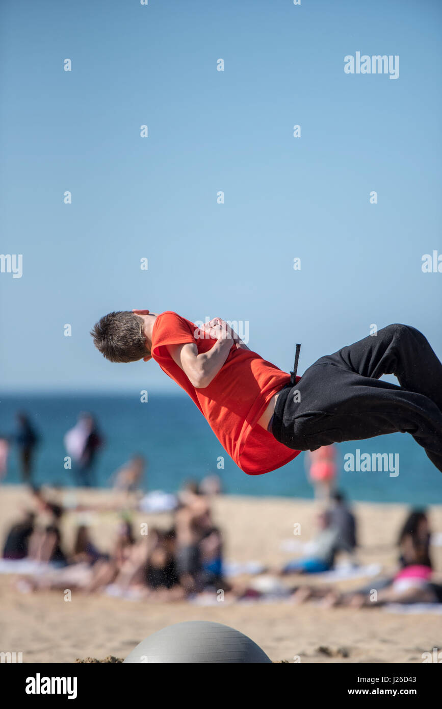 Kids are jumping very high on a beach and doing flip overs turning in ...
