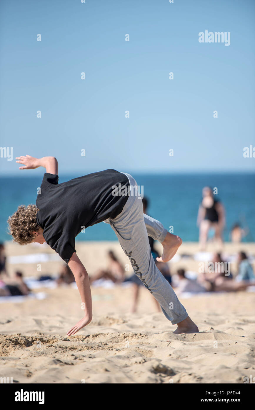 Kids are jumping very high on a beach and doing flip overs turning in ...