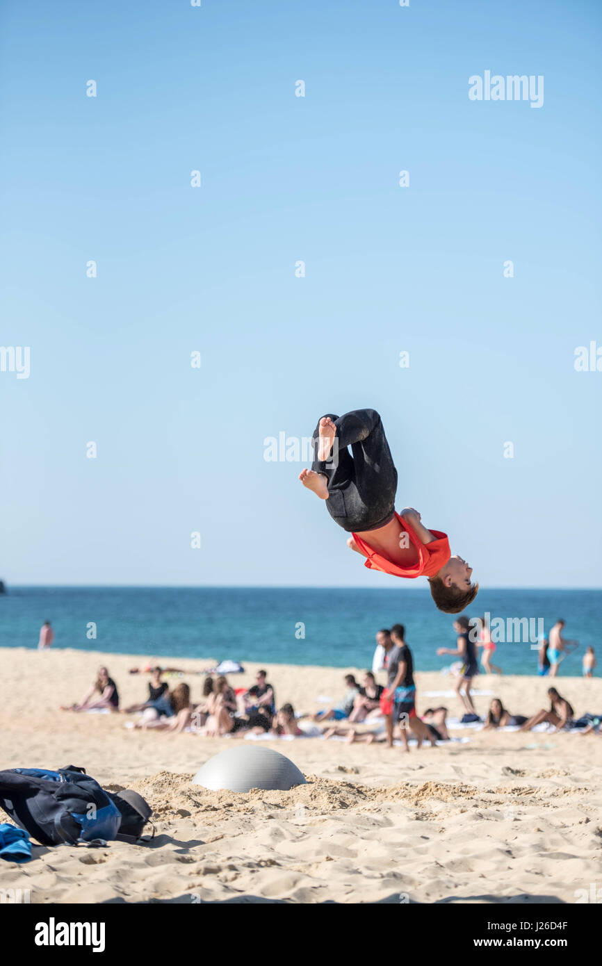 Kids are jumping very high on a beach and doing flip overs turning in ...