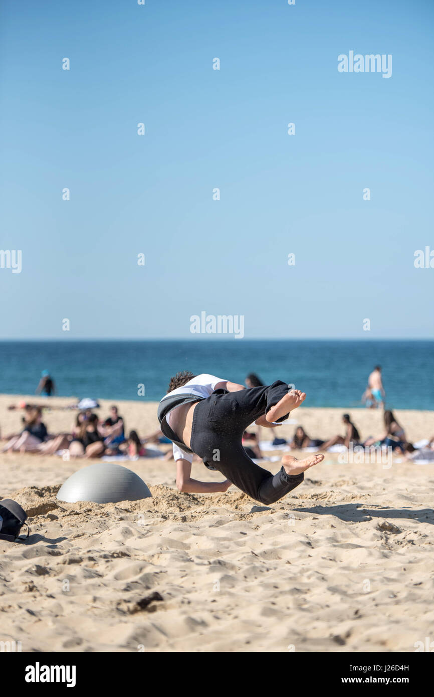 Kids are jumping very high on a beach and doing flip overs turning in ...