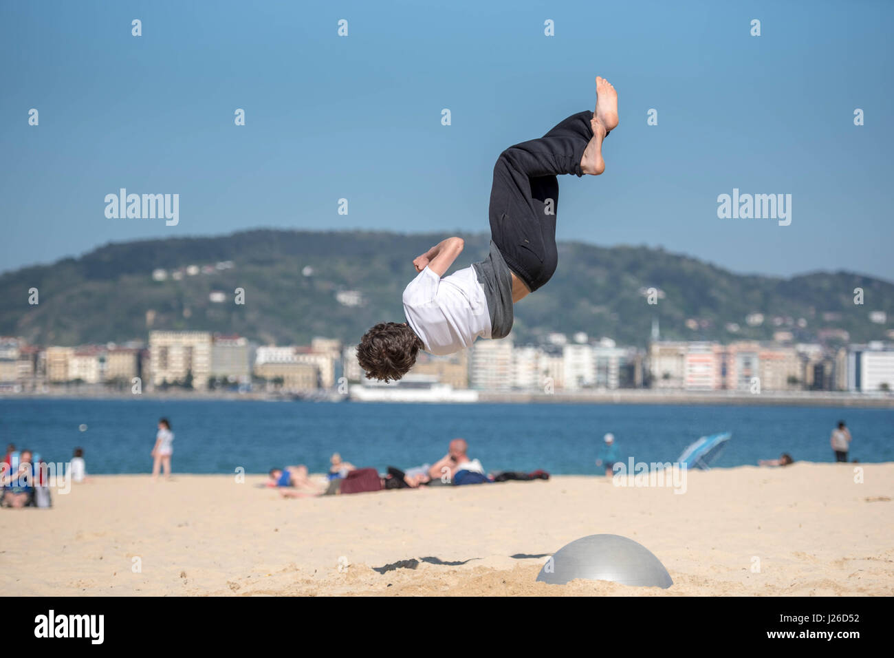 Kids are jumping very high on a beach and doing flip overs turning in ...