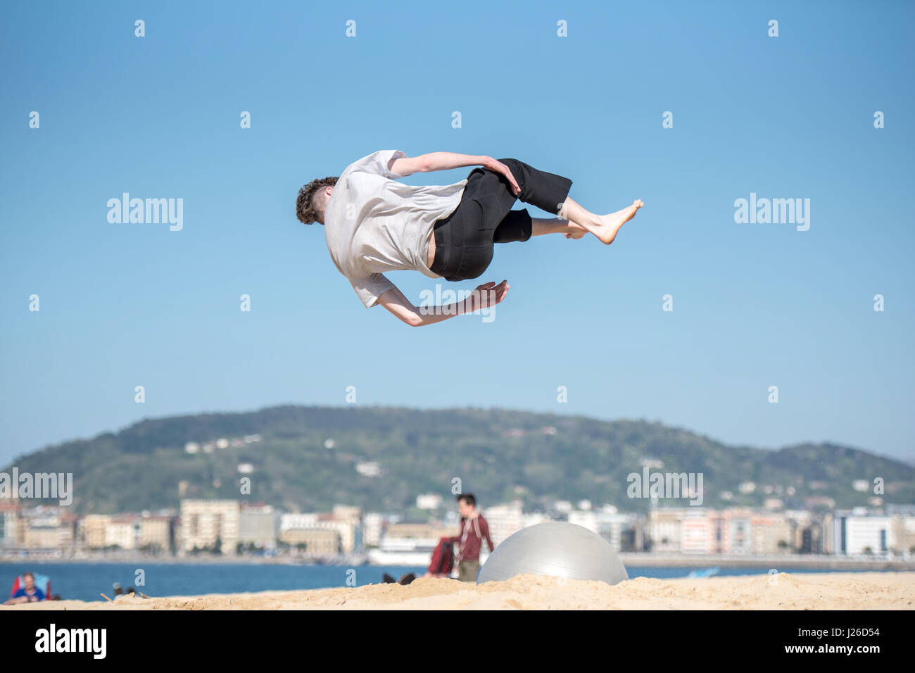 Kids are jumping very high on a beach and doing flip overs turning in ...