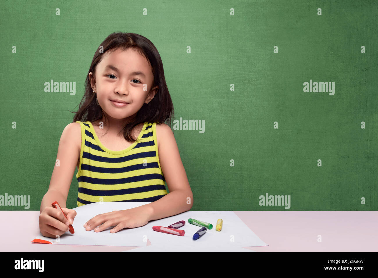 Portrait of asian kid drawing with colorful crayon against chalkboard ...