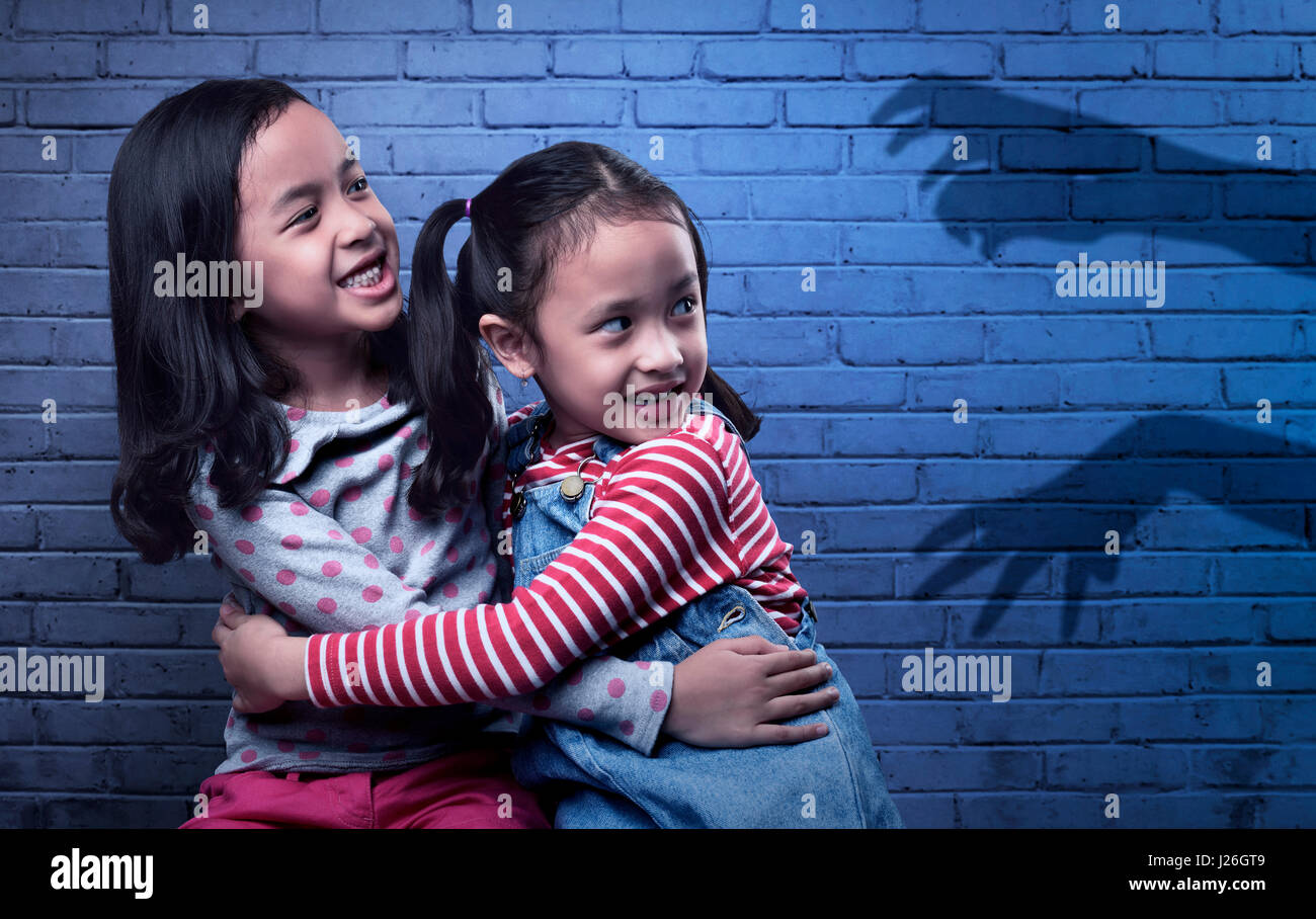 Scared two asian little girl looking at black ghost hand on wall ...