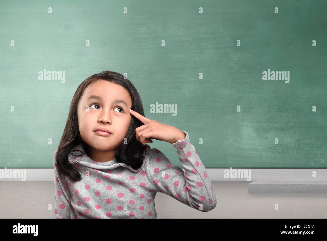Happy asian girl thinking with pensive expression against chalkboard ...
