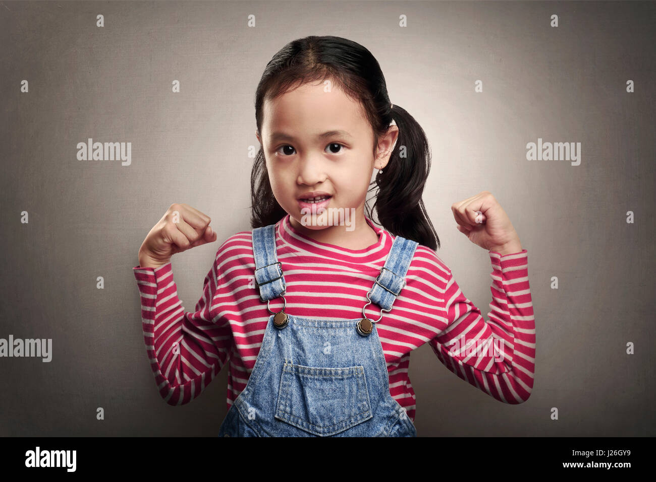 Attractive asian little girl showing her muscle on grey background ...