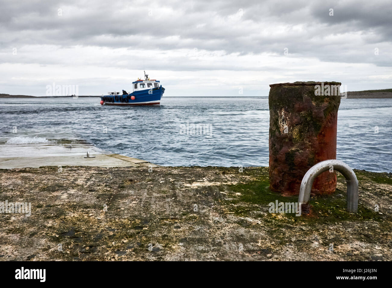 A small passenger motor boat approaches a slipway under grey skies ...