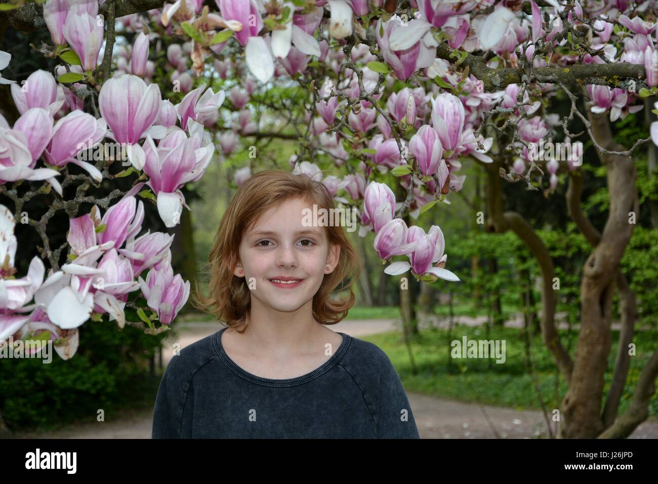 Girl stands under blossoming magnolia trees ( Magnoliaceae ) and smiles ...