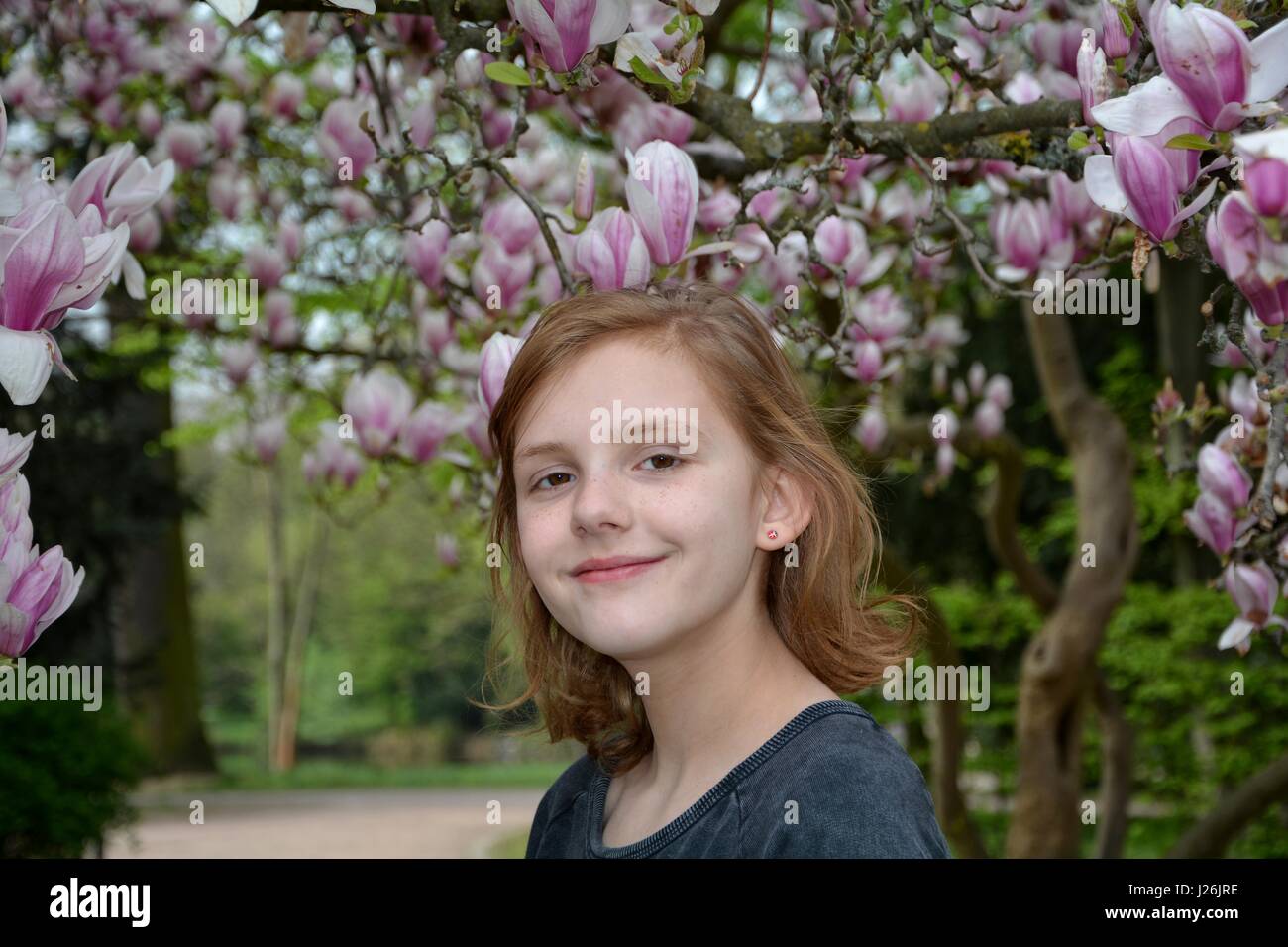 Girl stands under blossoming magnolia trees ( Magnoliaceae ) and smiles ...