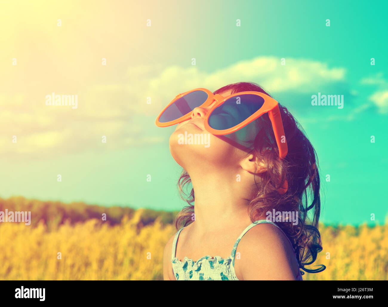 Happy little girl with big sunglasses looking at the sun in the wheat ...