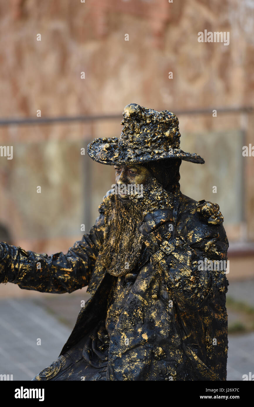 Street artist dressed as a gold statue collects money for living Stock ...