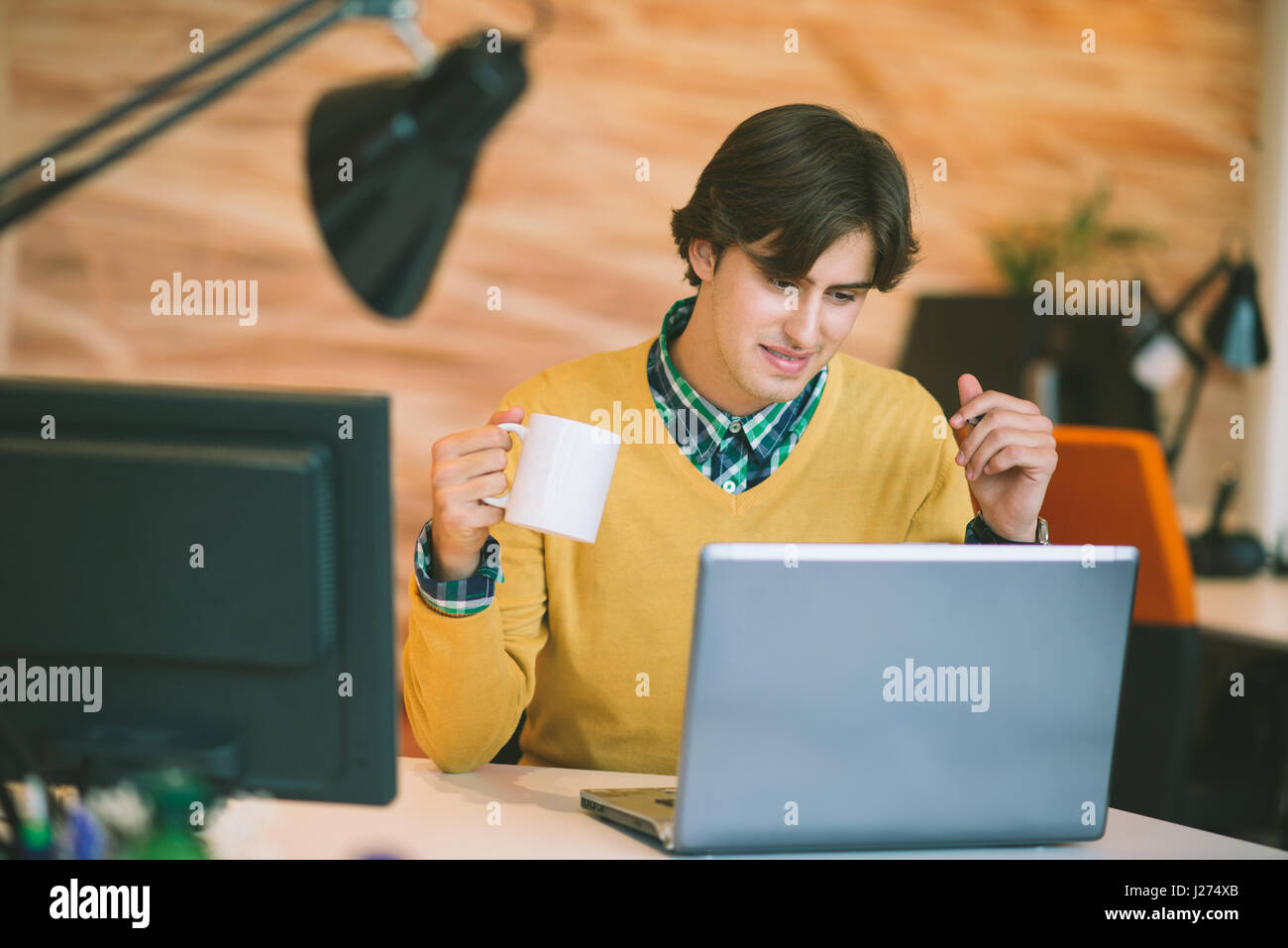 Portrait of young man sitting at his desk in the office Stock Photo - Alamy