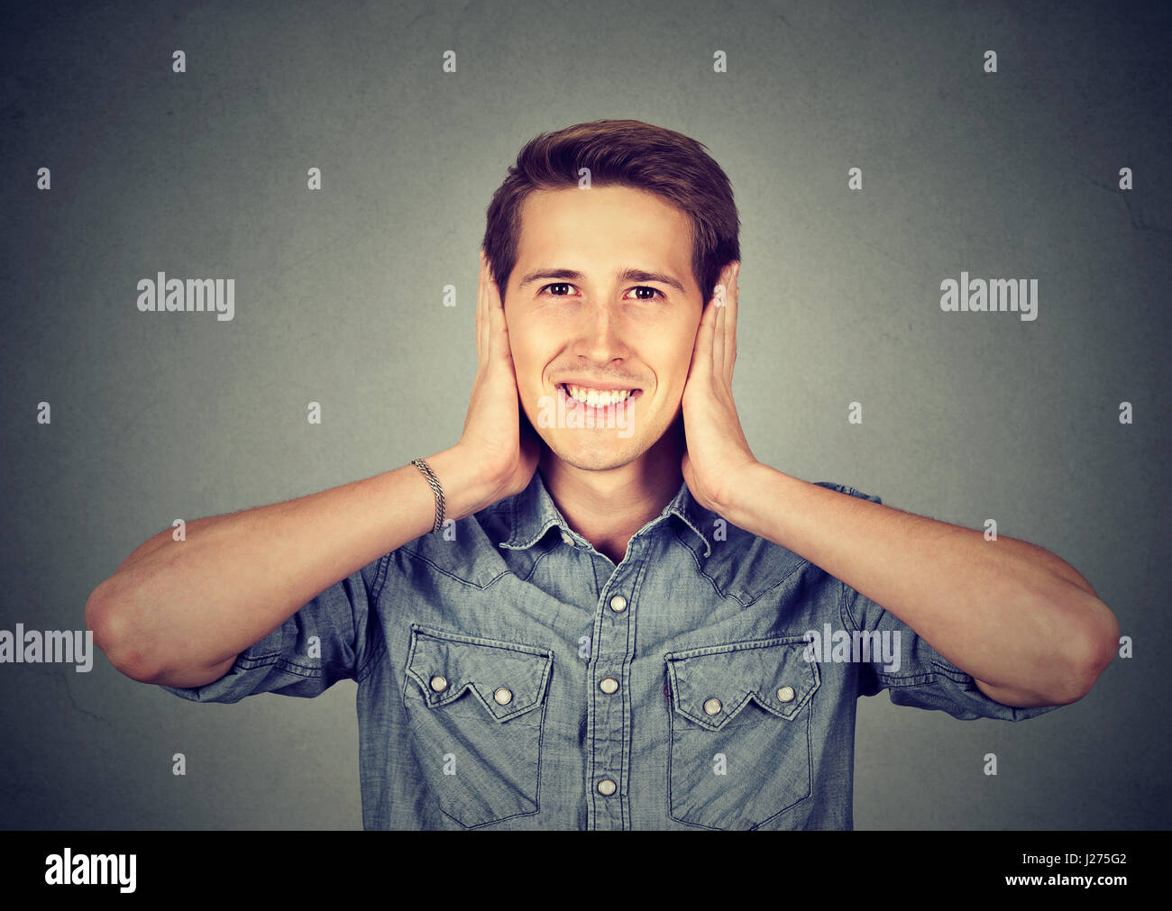 Handsome happy young man covering his ears with hands. Hear no evil ...