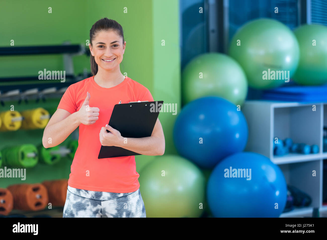 Portrait of smiling female fitness instructor writing in clipboard ...