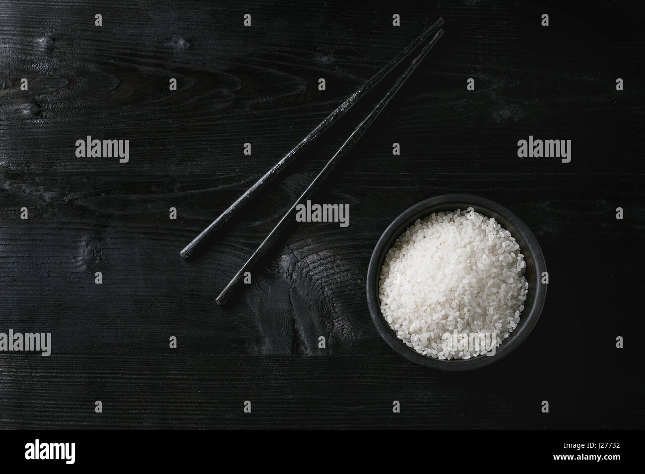 White sushi raw uncooked rice in black bowl with chopsticks over burnt ...
