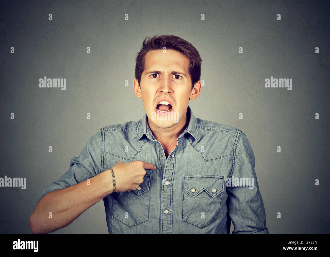 Angry, mad, unhappy young guy pointing at himself asking you mean me ...